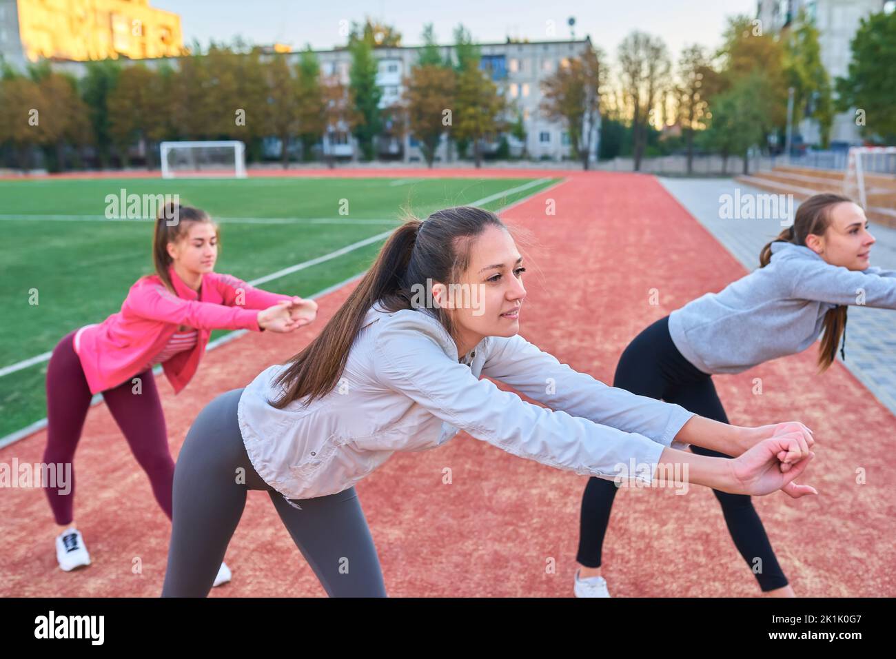Three girls doing stretching exercises at the football stadium Stock ...