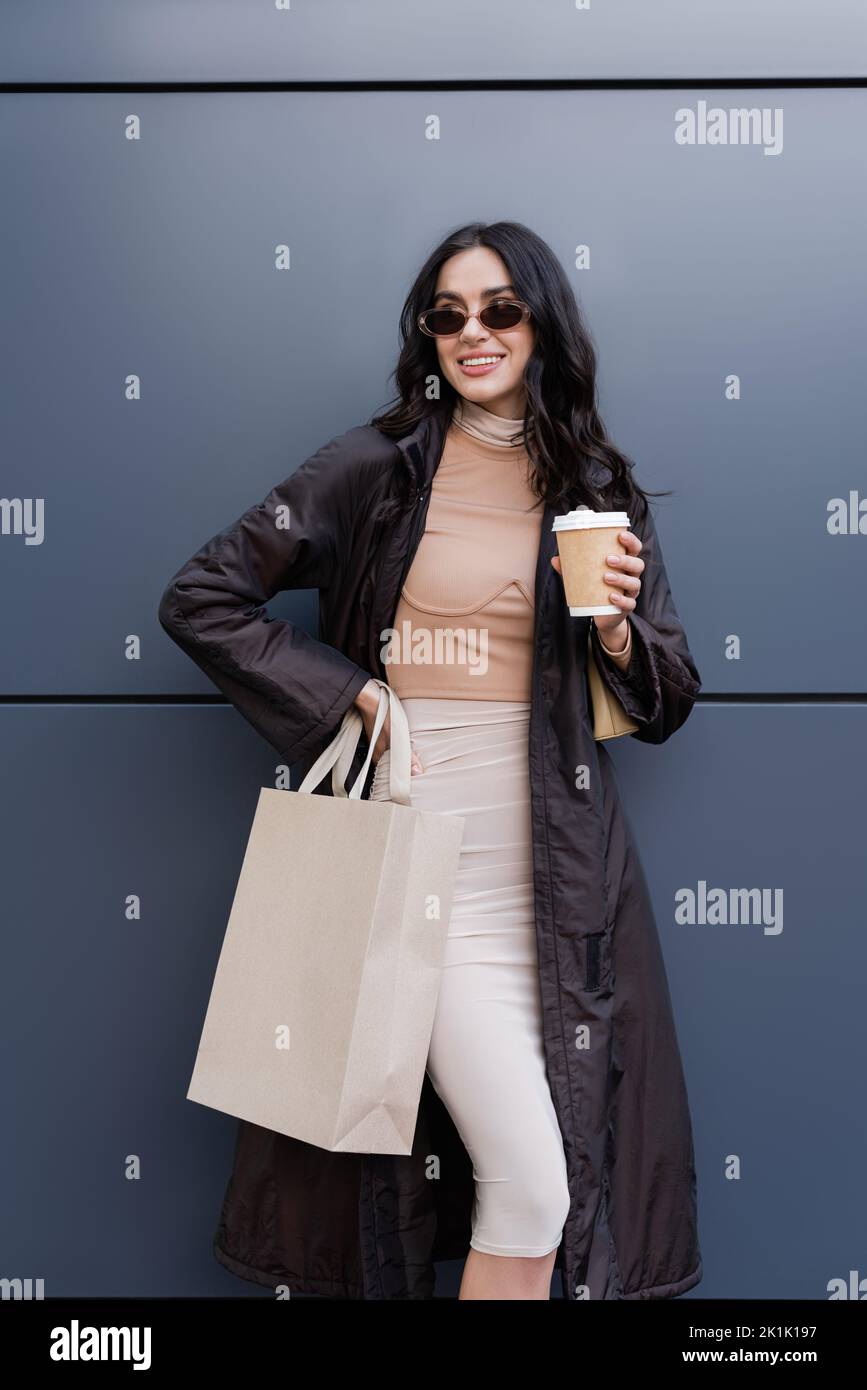happy young woman in stylish outfit and sunglasses holding paper cup ...
