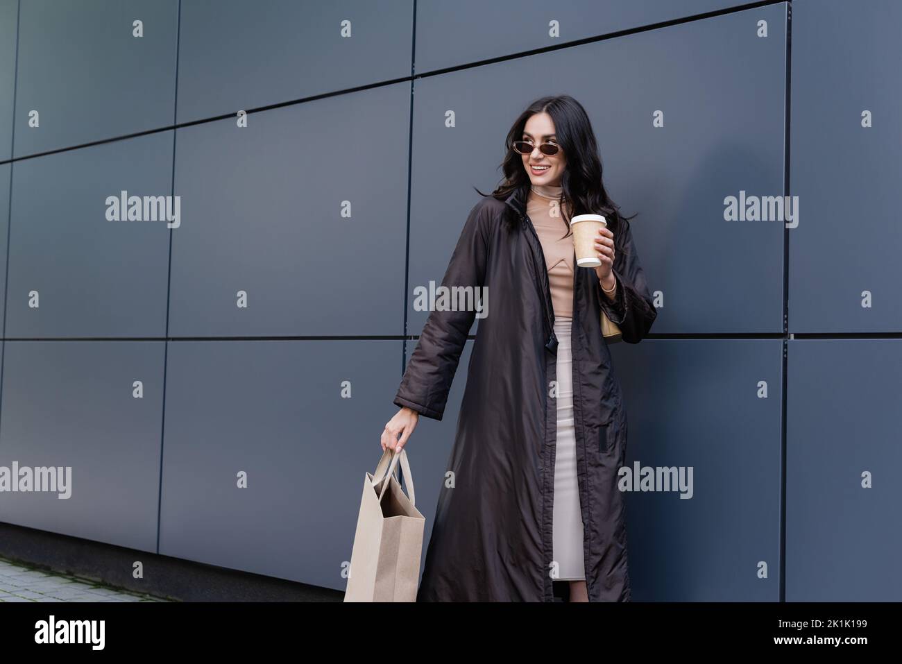 cheerful young woman in stylish outfit and sunglasses holding paper cup ...