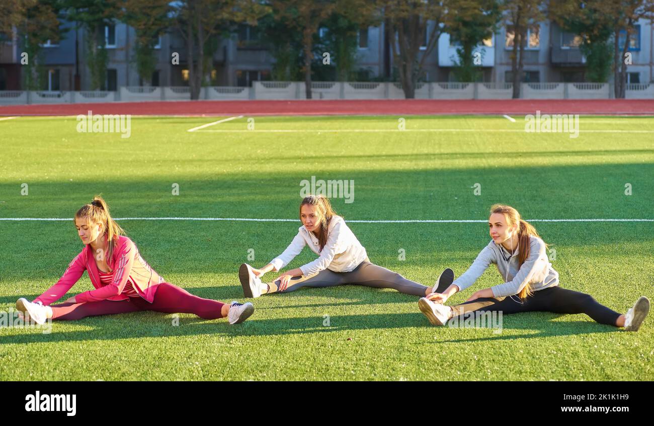 Three girls doing stretching exercises at the football stadium Stock ...