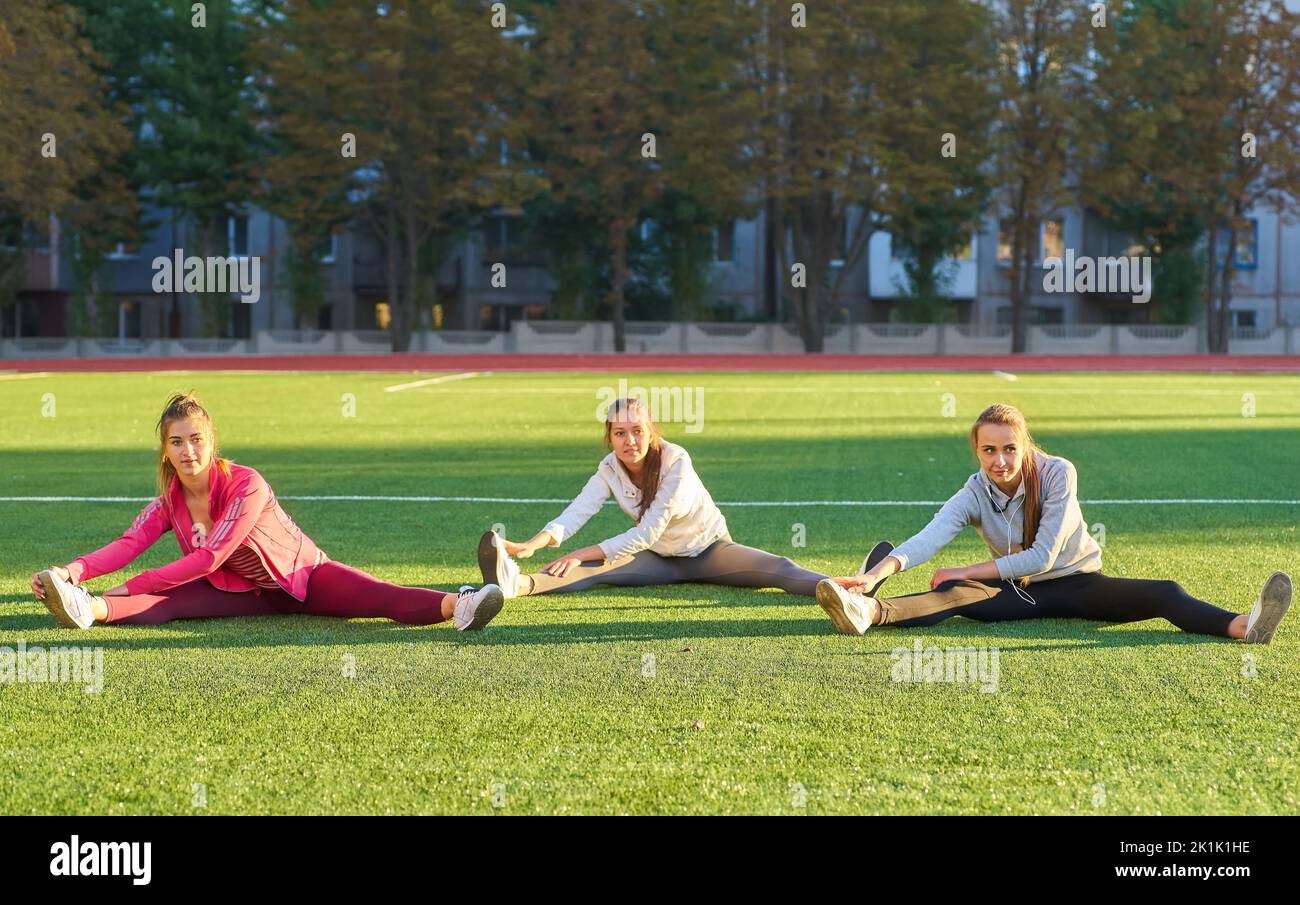 Three girls doing stretching exercises at the football stadium Stock ...