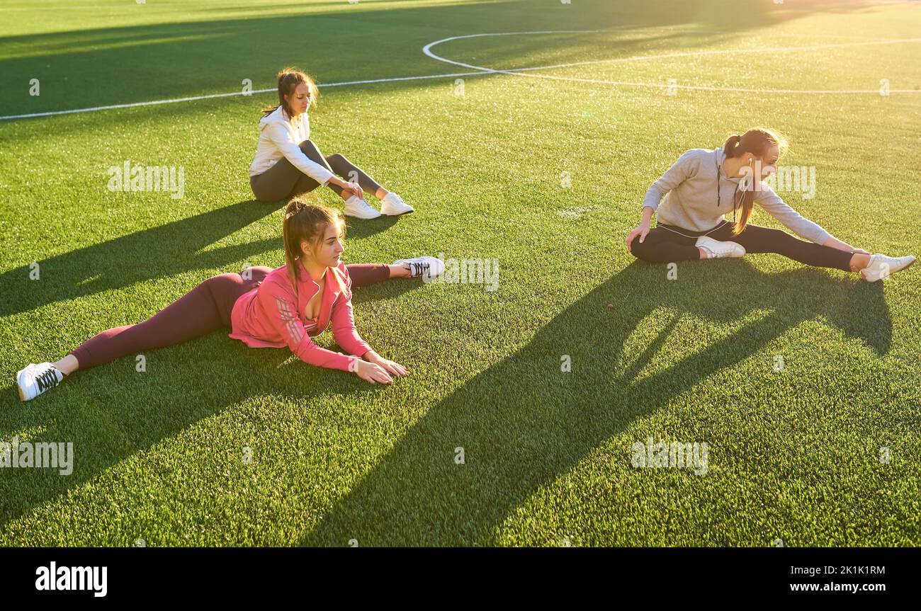 Three girls doing stretching exercises at the football stadium Stock ...