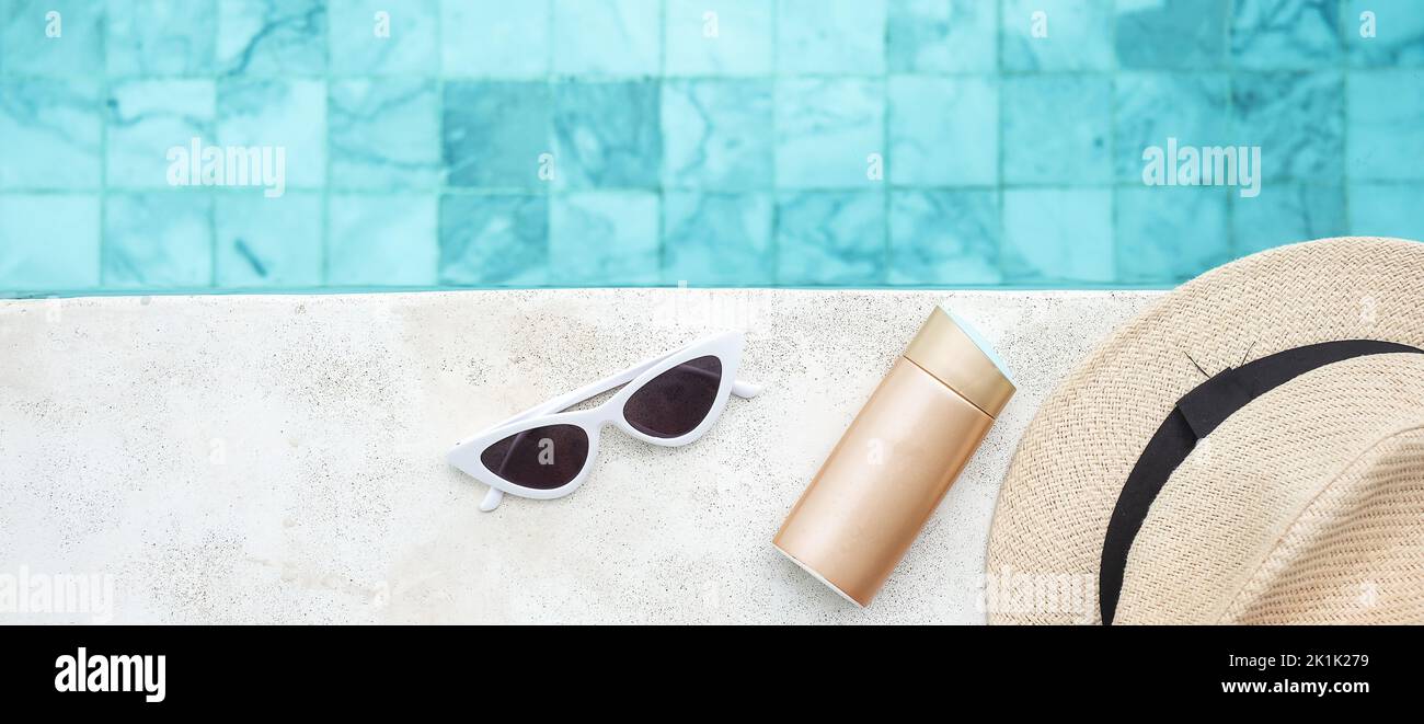 white sunglasses, sunscreen bottle and hat near swimming pool in luxury ...