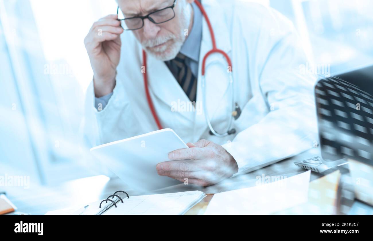 Male senior doctor using digital tablet in medical office; light effect ...