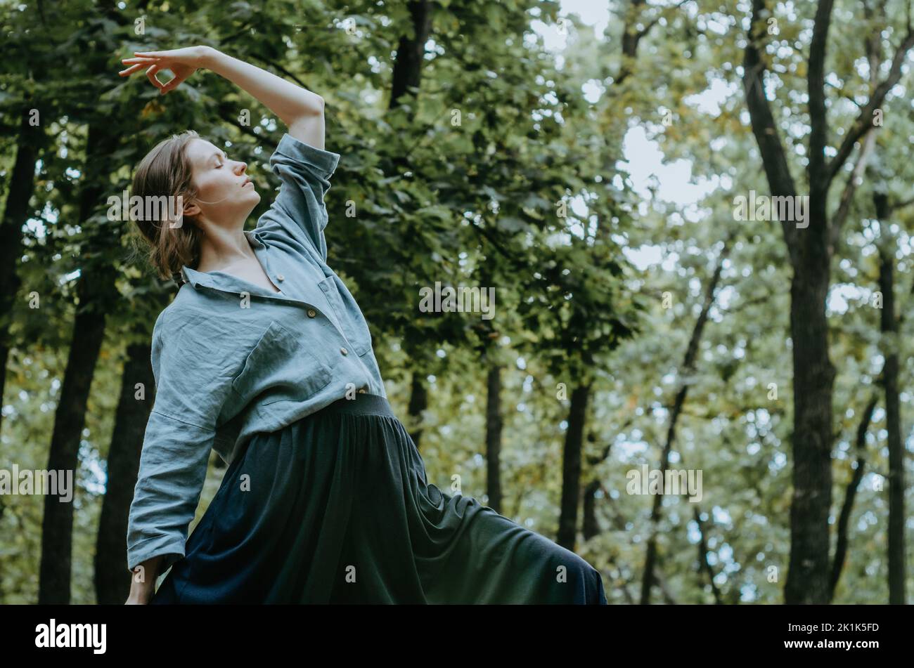 Woman doing yoga peaceful warrior pose with forest trees background ...