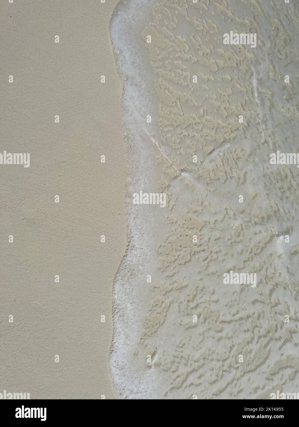 A vertical view of a frothy white wave washing on white sandy beach on ...