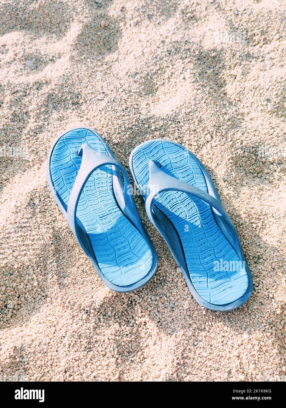 A vertical shot of two blue sandals on the sand on a beach in sunny ...