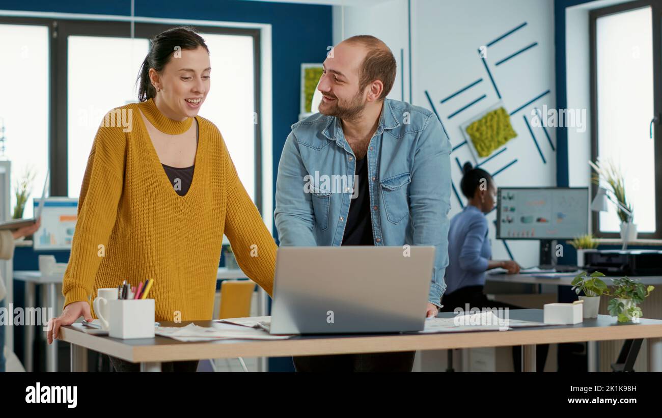 Smiling coworkers in office looking at laptop screen comparing business ...