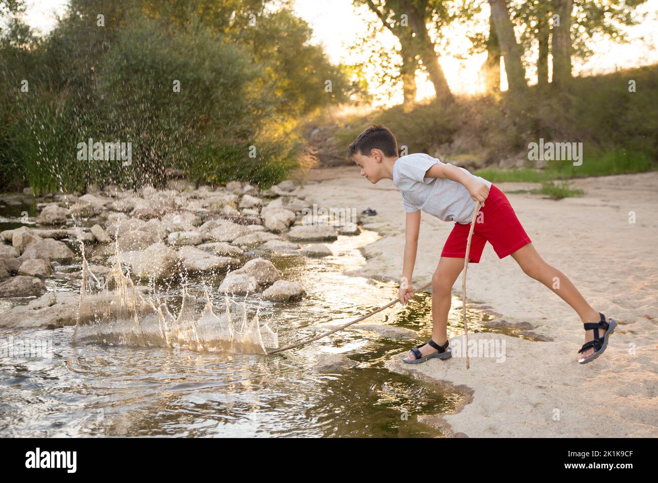 child plays in the river splashing in the water with a stick Stock ...