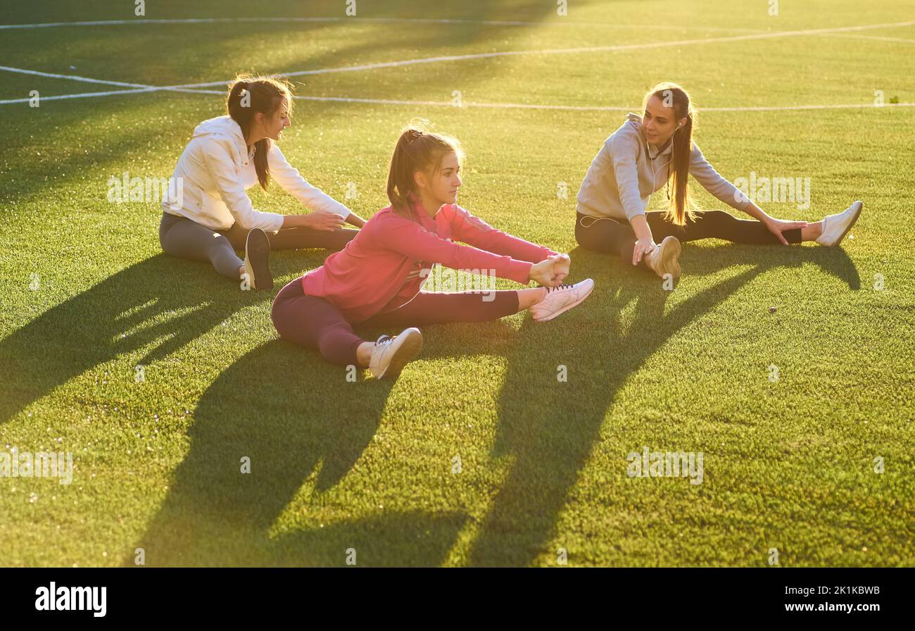 Three girls doing stretching exercises at the football stadium Stock ...
