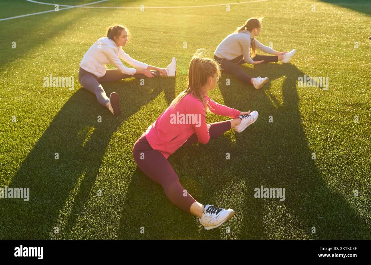 Three girls doing stretching exercises at the football stadium Stock ...