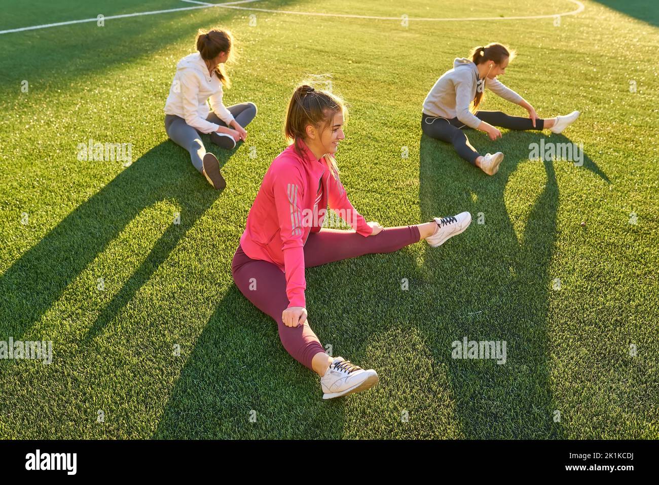 Three girls doing stretching exercises at the football stadium Stock ...