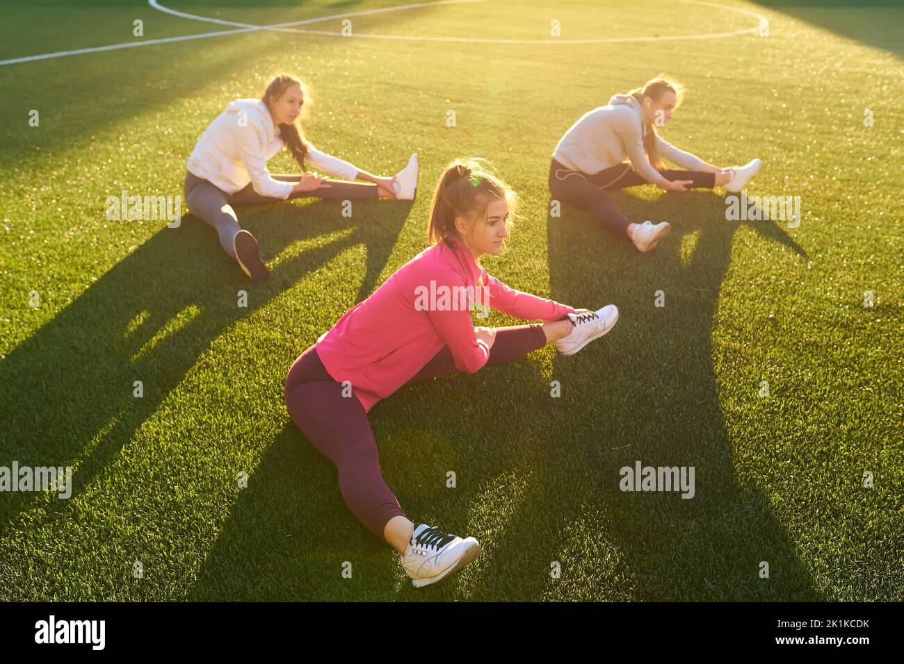 Three girls doing stretching exercises at the football stadium Stock ...