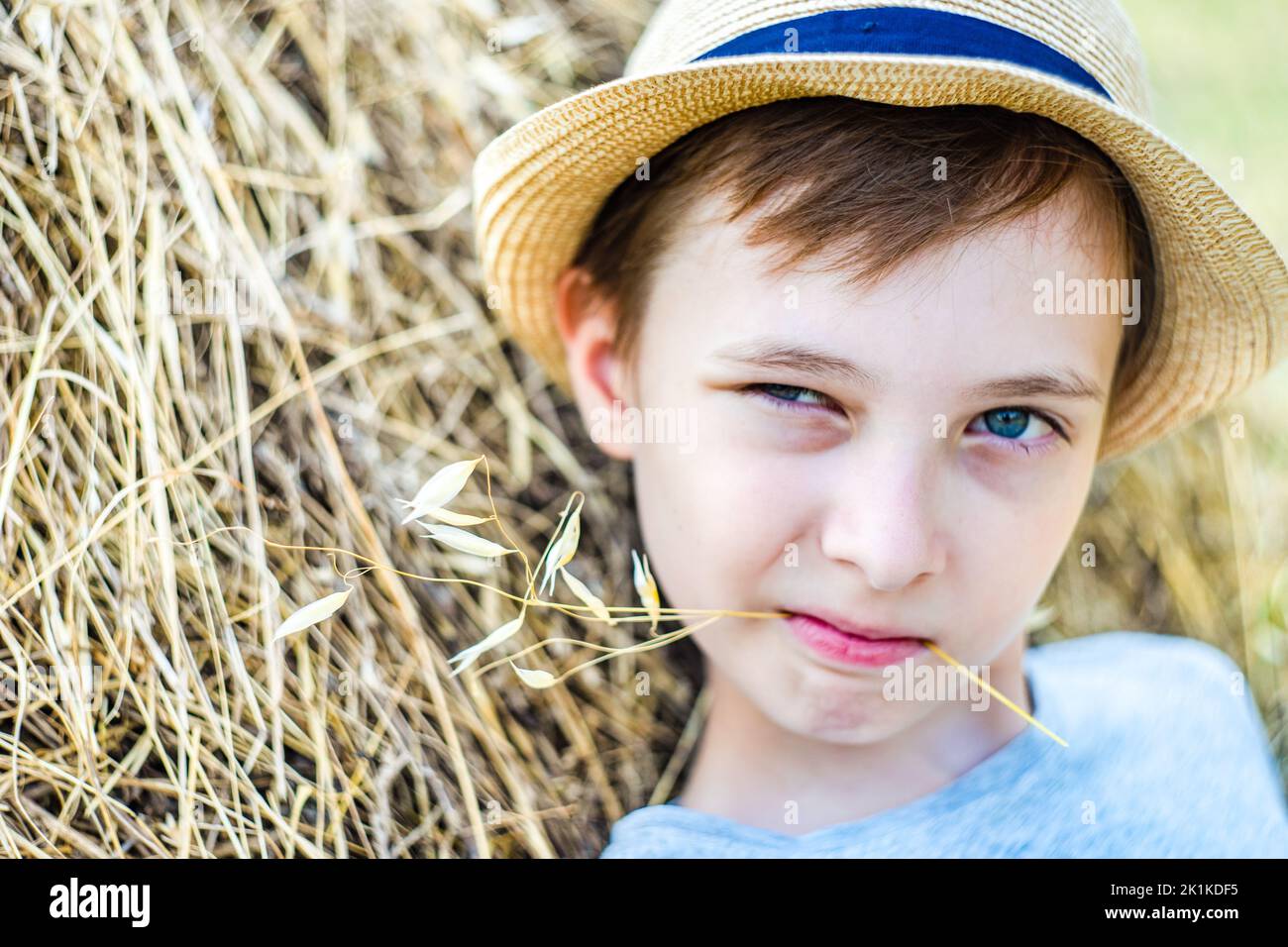 Portrait of a boy leaning against a hay stack chewing a piece of straw ...