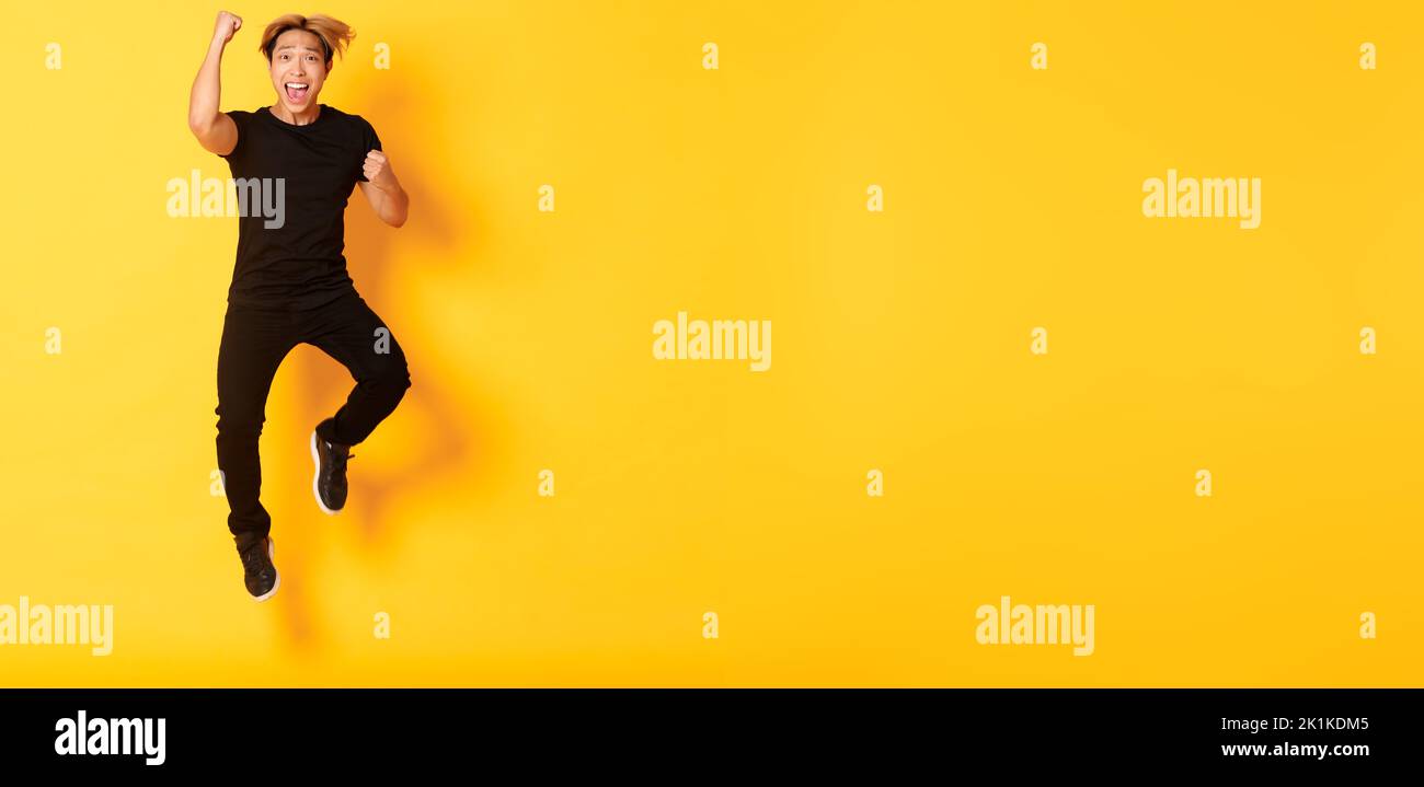 Full-length of happy attractive asian guy in black clothes jumping and ...