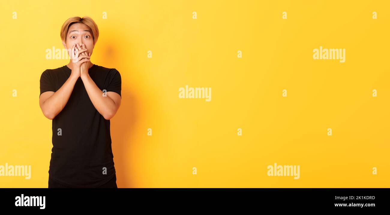 Portrait of surprised asian handsome guy with blond hair, cover mouth ...