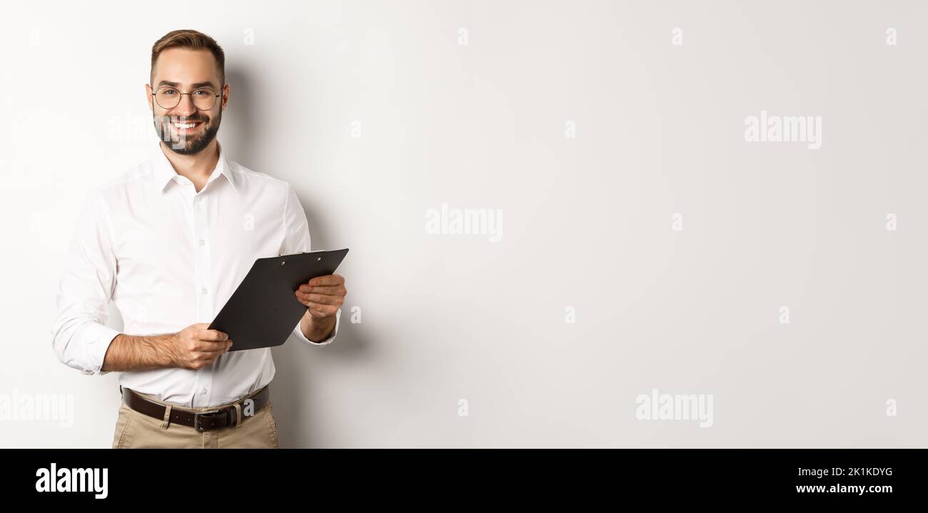 Handsome manager in glasses working, using clipboard, standing over ...