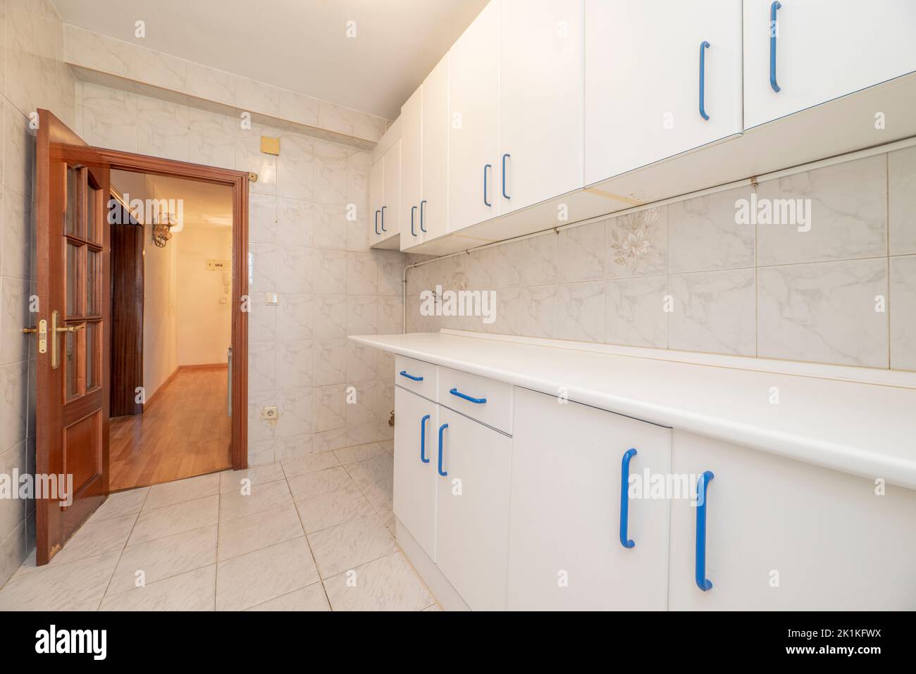 Long kitchen with white wooden countertops, white cabinets and blue ...
