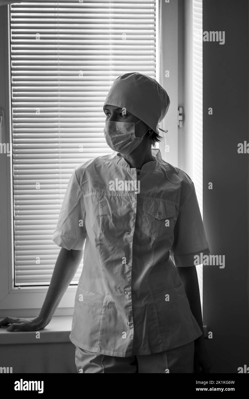 A woman doctor in a mask stands at a hospital window. Black and white ...