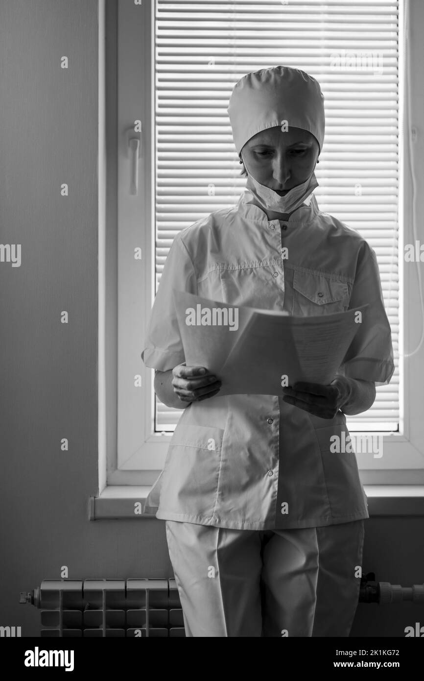 A female doctor stands at the window of the hospital reading documents ...