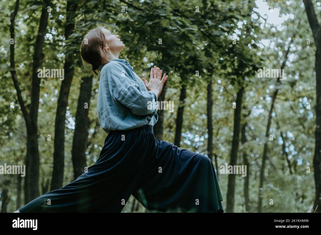 Woman doing yoga high lunge with namaste hands in the forest, looking ...