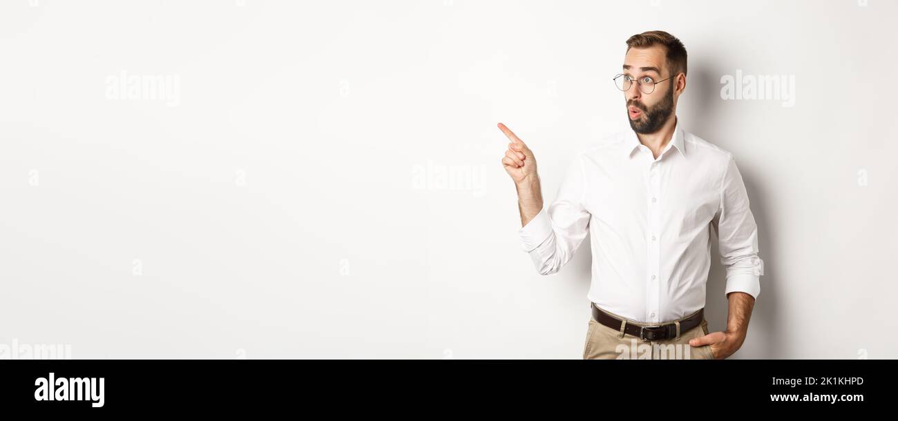Intrigued young man in glasses pointing finger left, looking at promo ...