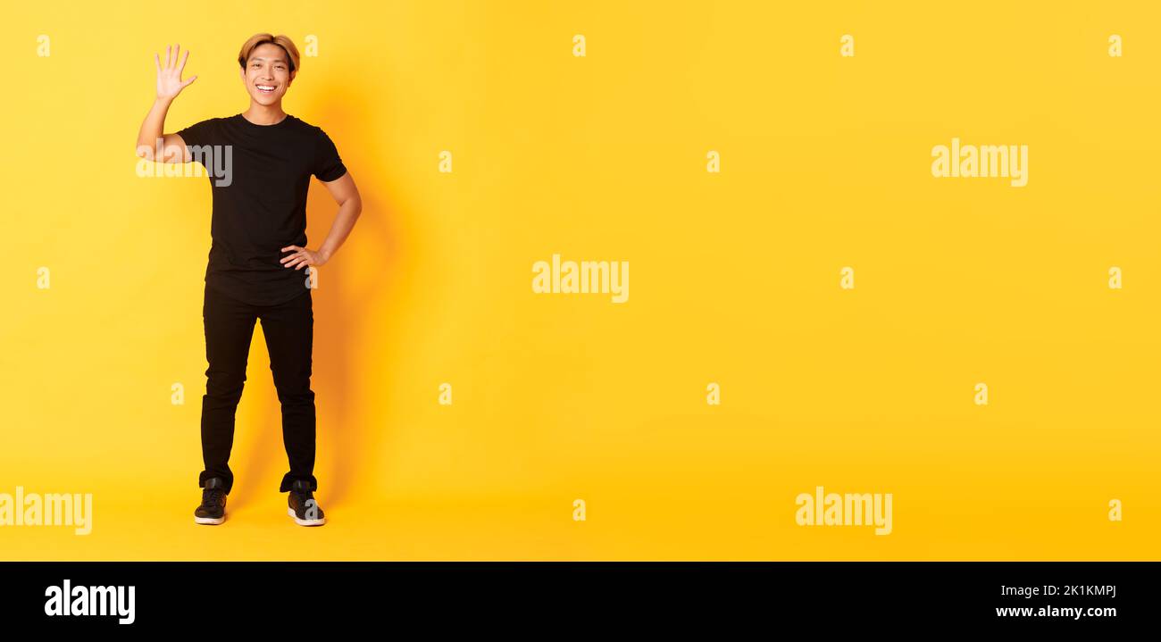 Full-length of friendly handsome asian man waving hand in hello ...