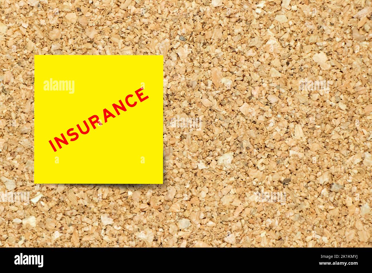 Yellow note paper with word insurance on cork board background with ...