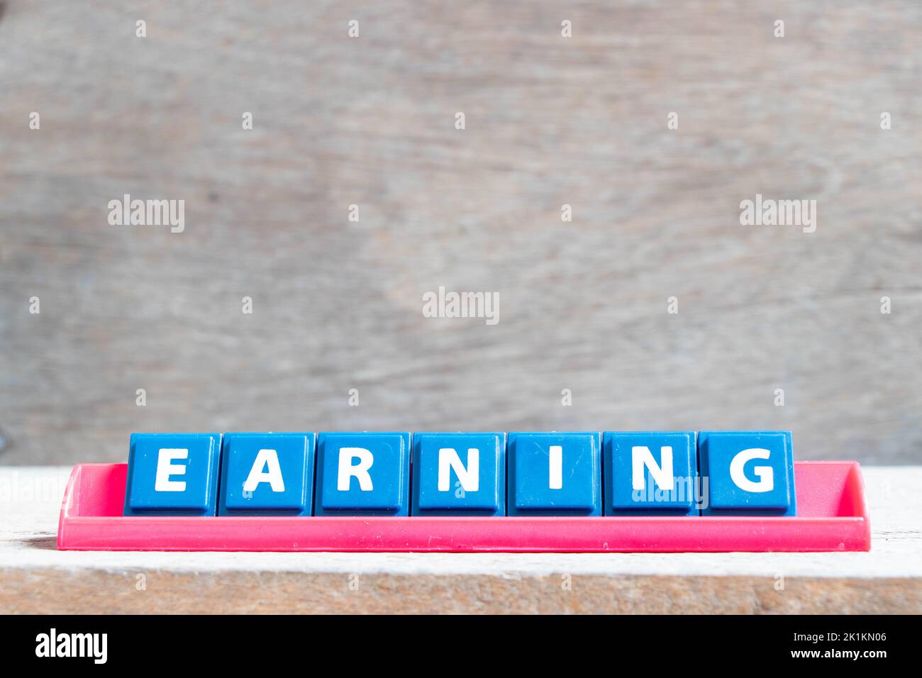 Tile alphabet letter with word earning in red color rack on wood ...