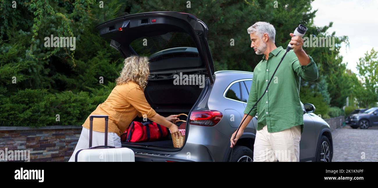 Man holding power supply cable, while his wife waiting for car charging ...
