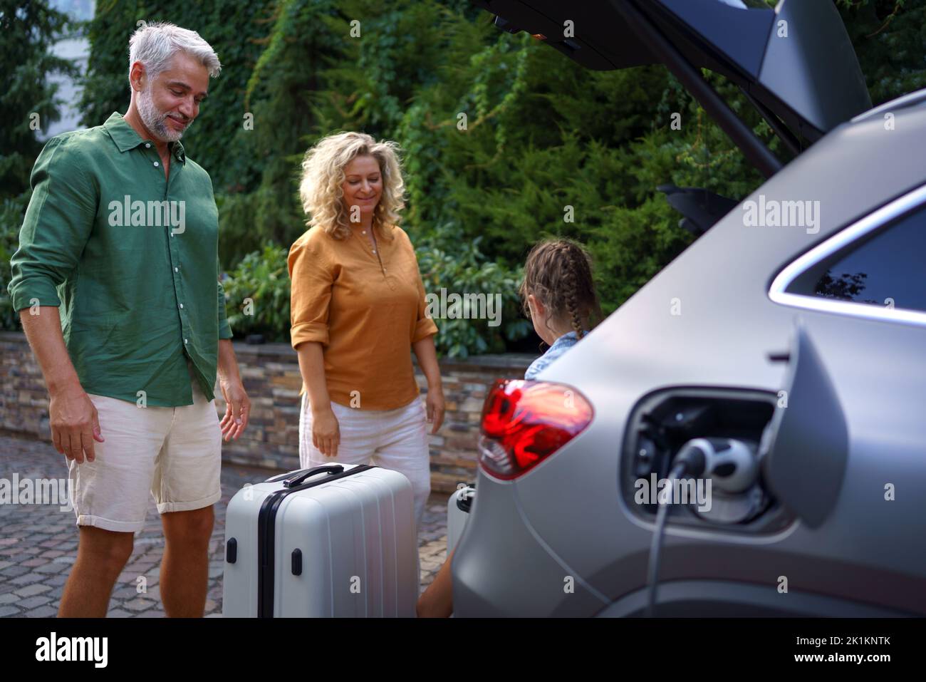 Family with little children loading car and waiting for charging car ...