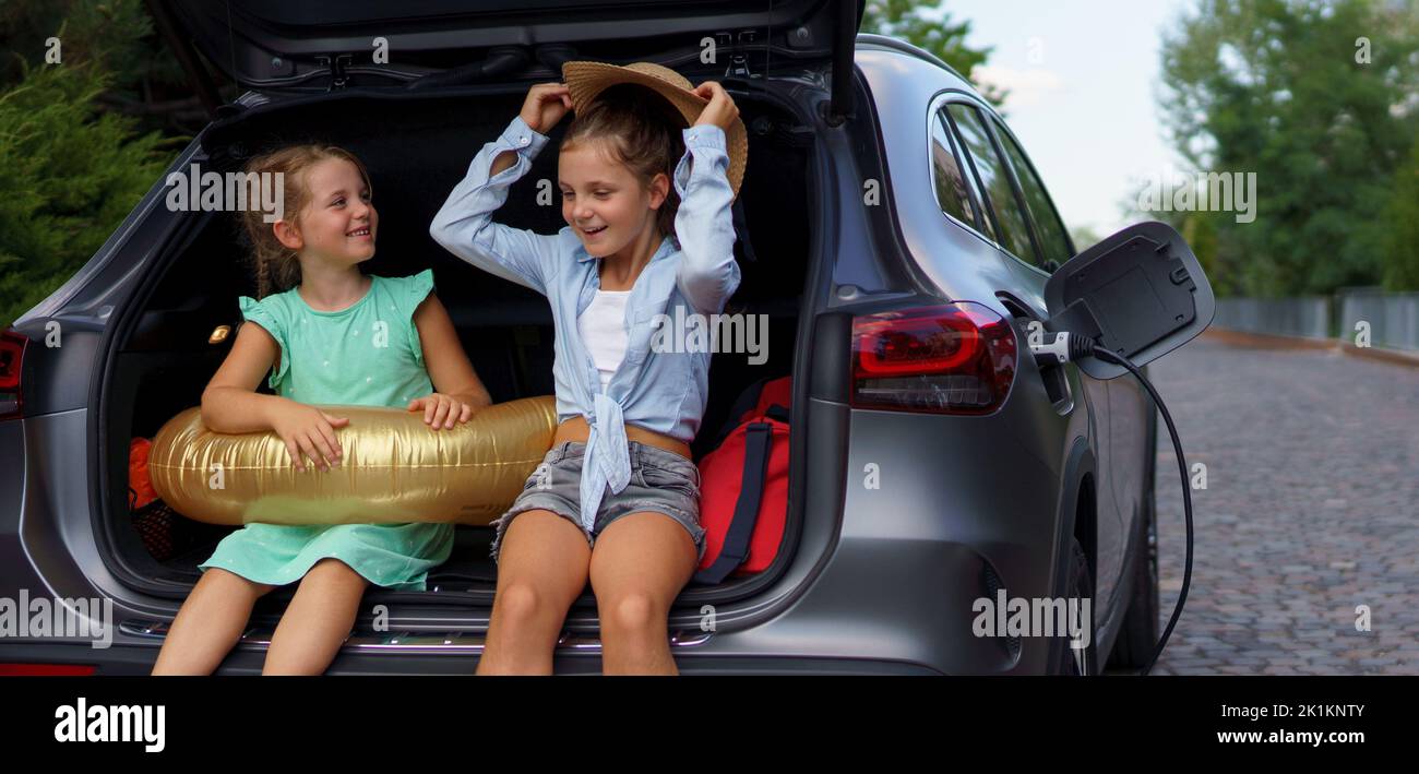 Cute little sisters sitting in trunk while waiting for charging car ...