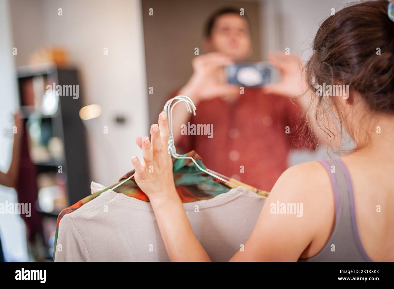 A charming young couple trying on clothes and having fun standing ...