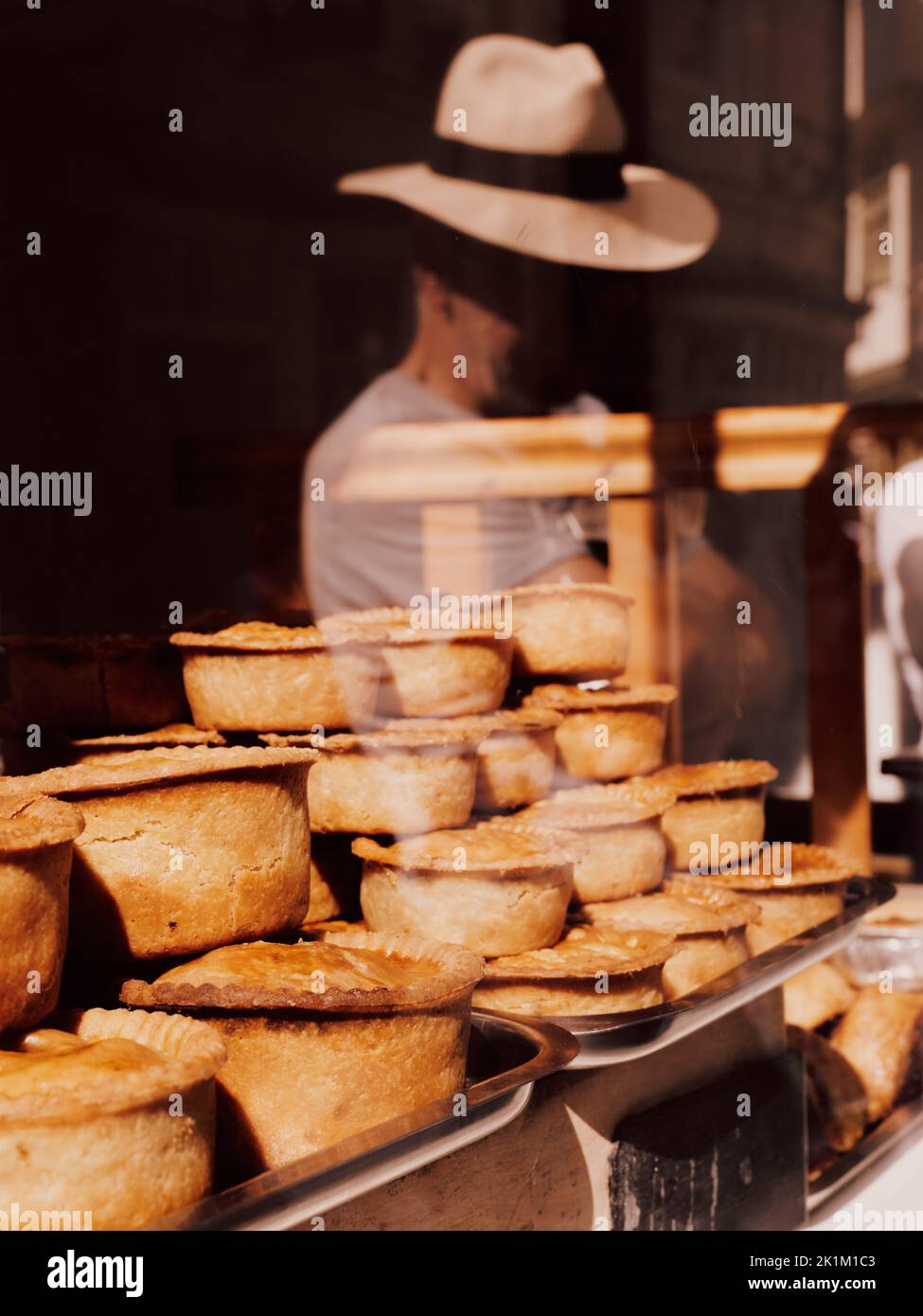 Traditional pork pies in a Pie shop window with a man in a summer hat ...
