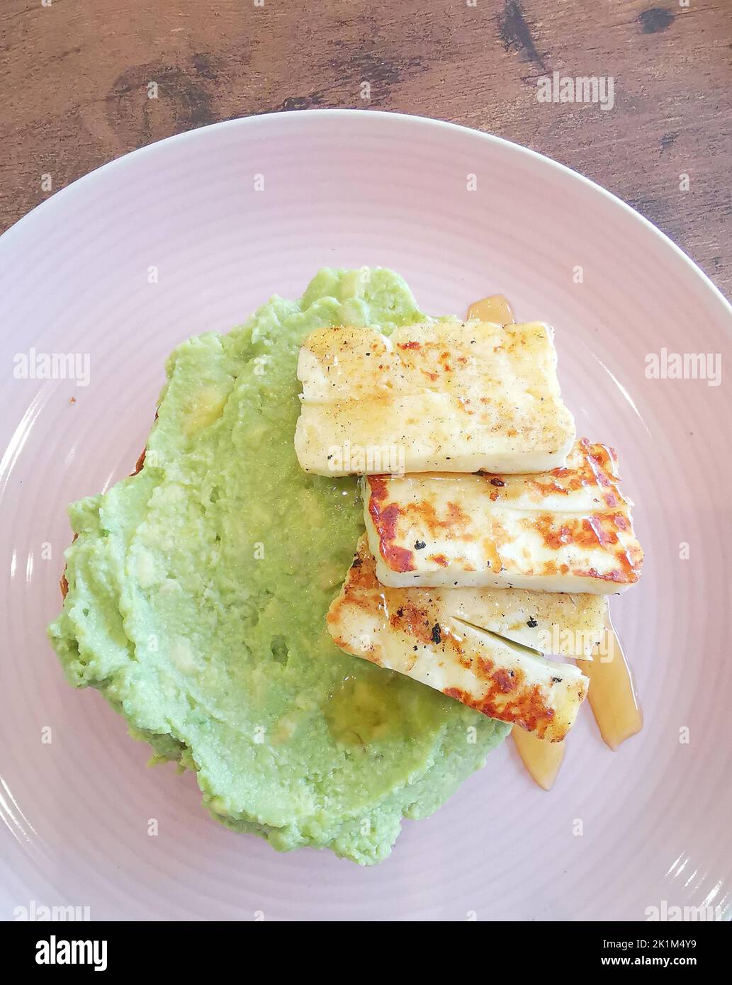 Smashed avocado on toast with grilled hallumi and honey on white plate ...