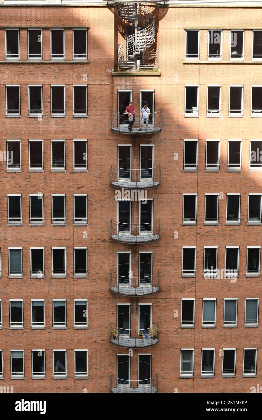 The vertical view of two men standing on the balcony of a brick-built ...