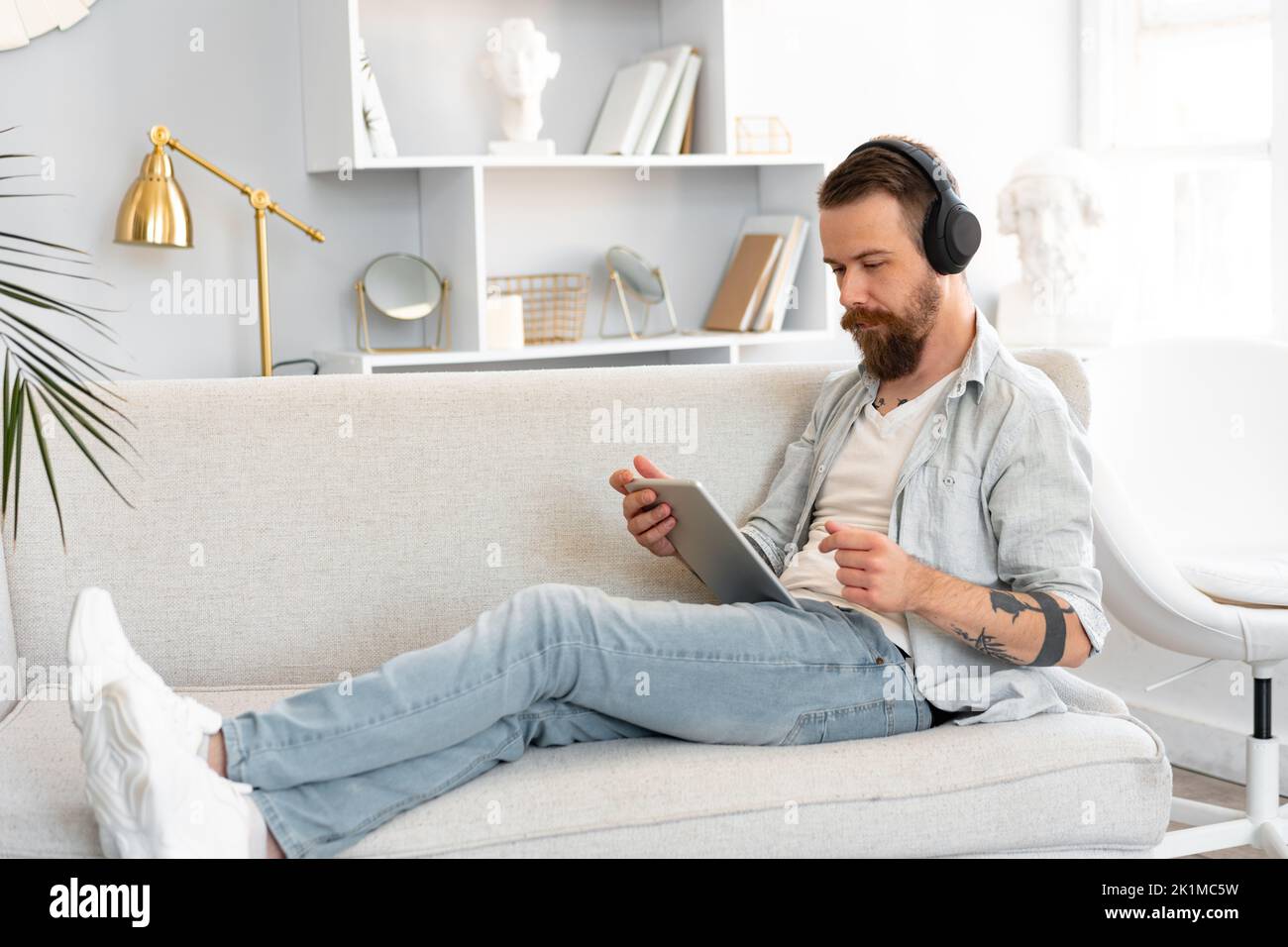 Handsome bearded man using digital tablet while resting on couch at ...