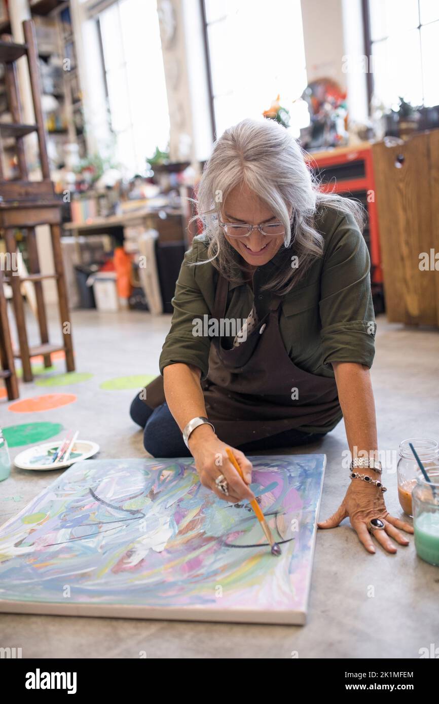 Mature woman painting on floor of studio Stock Photo - Alamy
