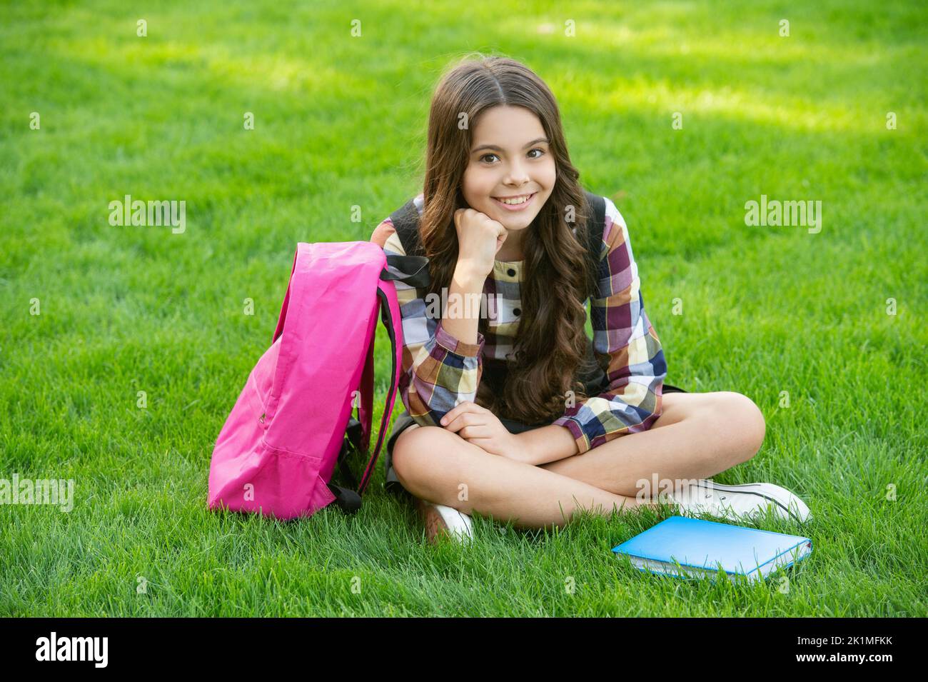 Happy teen girl sitting on grass after school, education. back to ...