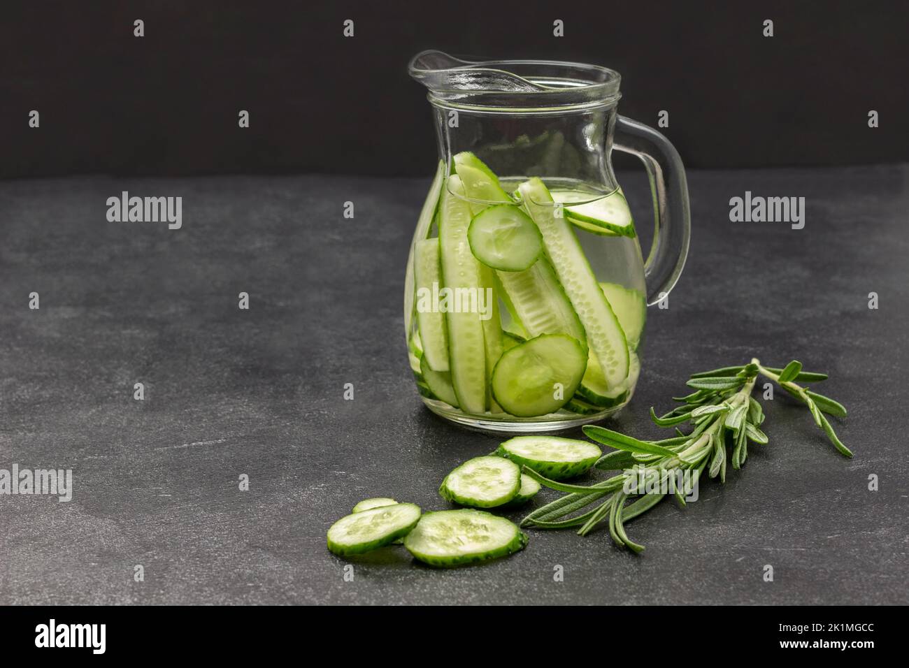 Cucumber infused water in glass jug. Sprig of rosemary on table. Copy ...