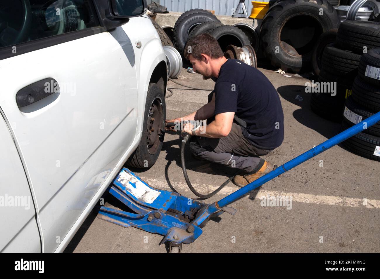 Young man worker changing a tyre on the wheel of a car in Llandovery ...