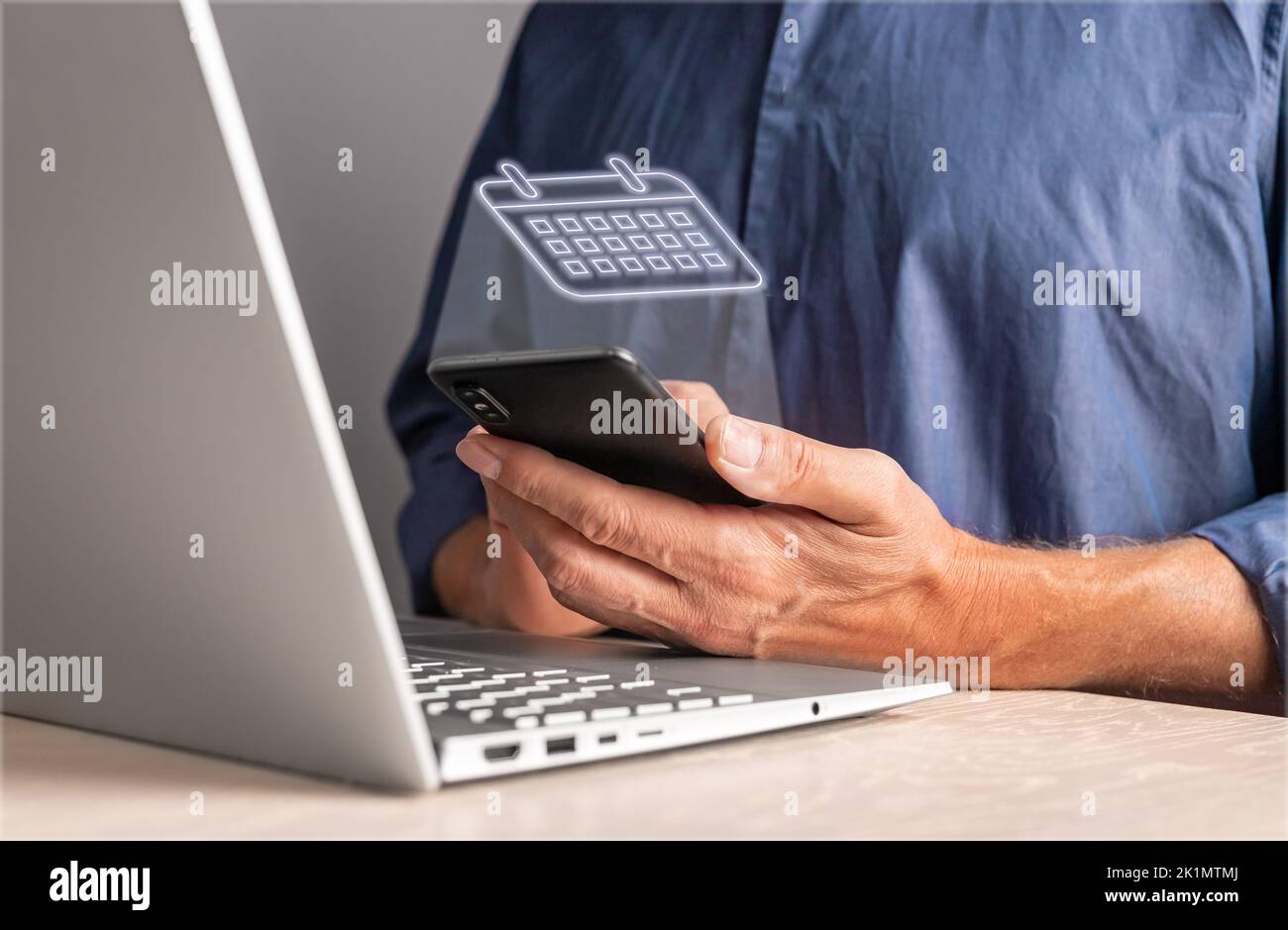 Man using calendar on phone while sitting at table with laptop. Work ...