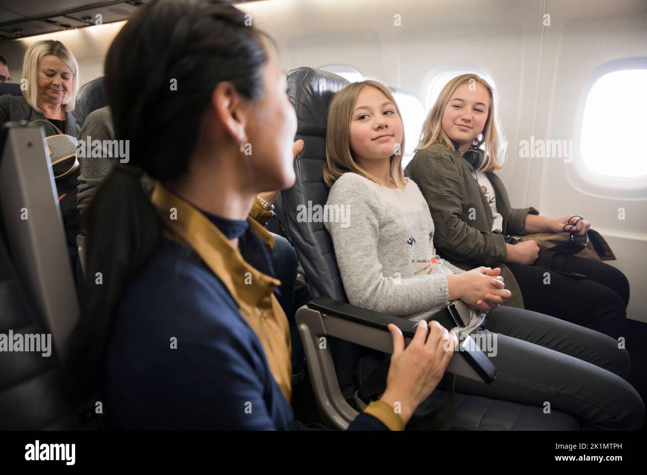 Flight attendant talking to girls on airplane Stock Photo - Alamy
