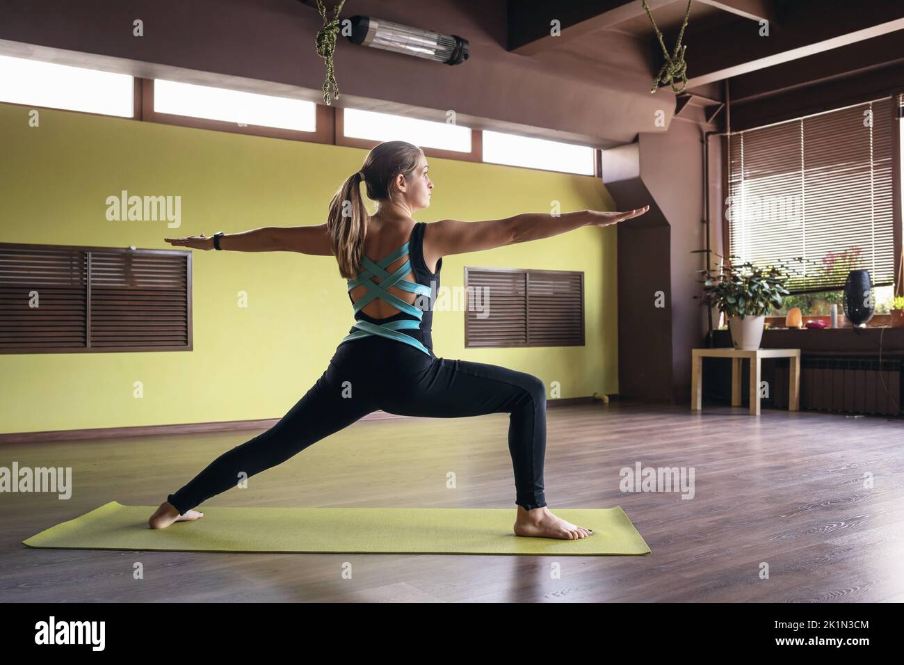 A woman practicing yoga, performs the exercise virabhadrasana, warrior pose, trains in the ...