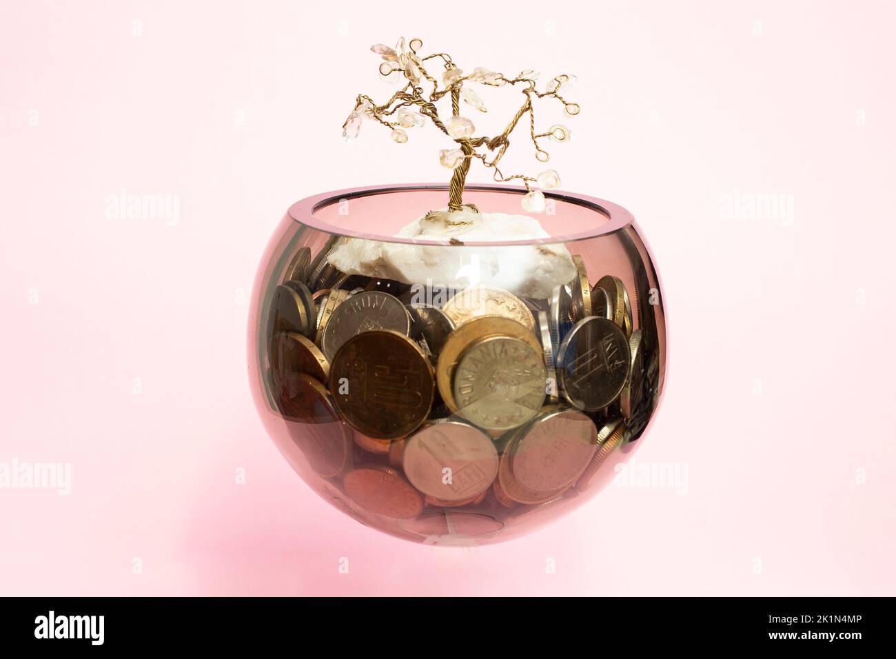Glass bowl full of coins with a wire tree on top, levitating on pink ...