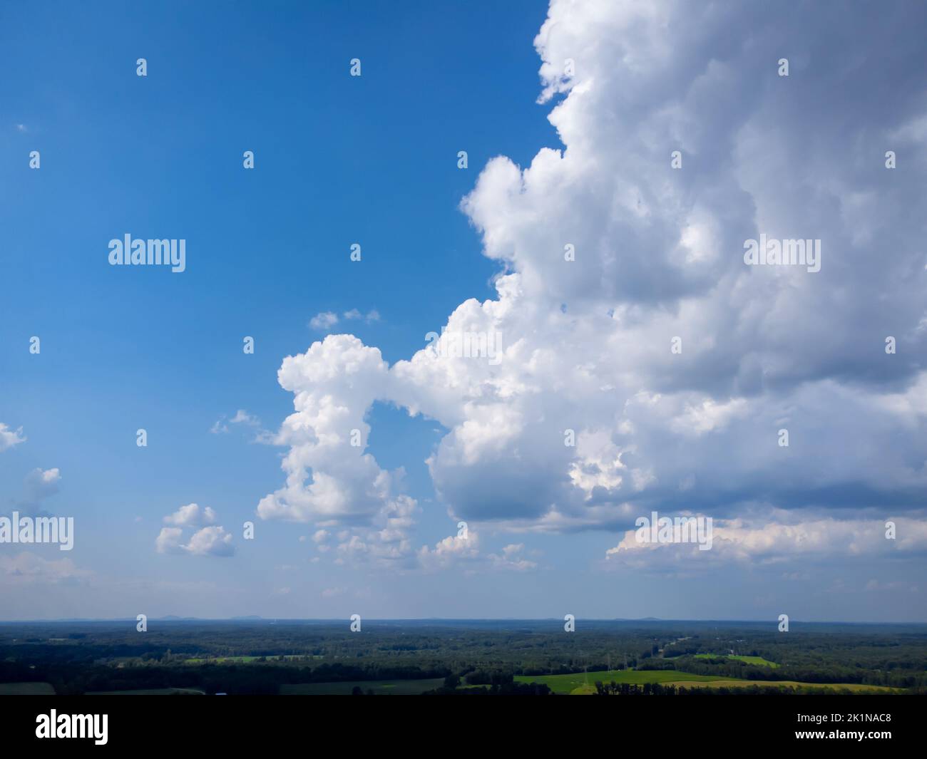 Towering cumulonimbus clouds over green rural landscape with deep blue ...