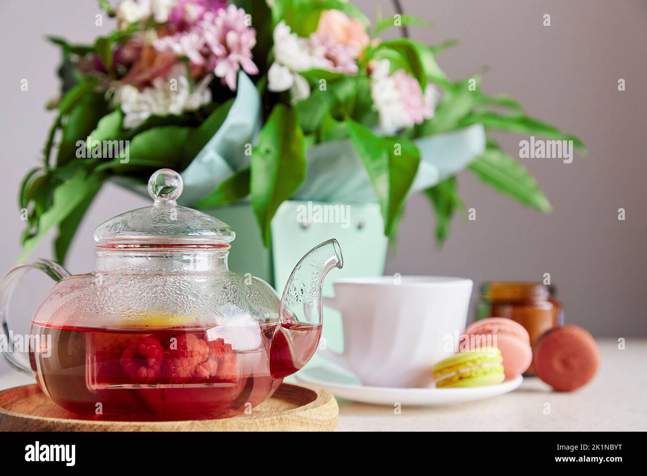 Natural herbal raspberry red tea in glass teapot, macaroons and bouquet ...