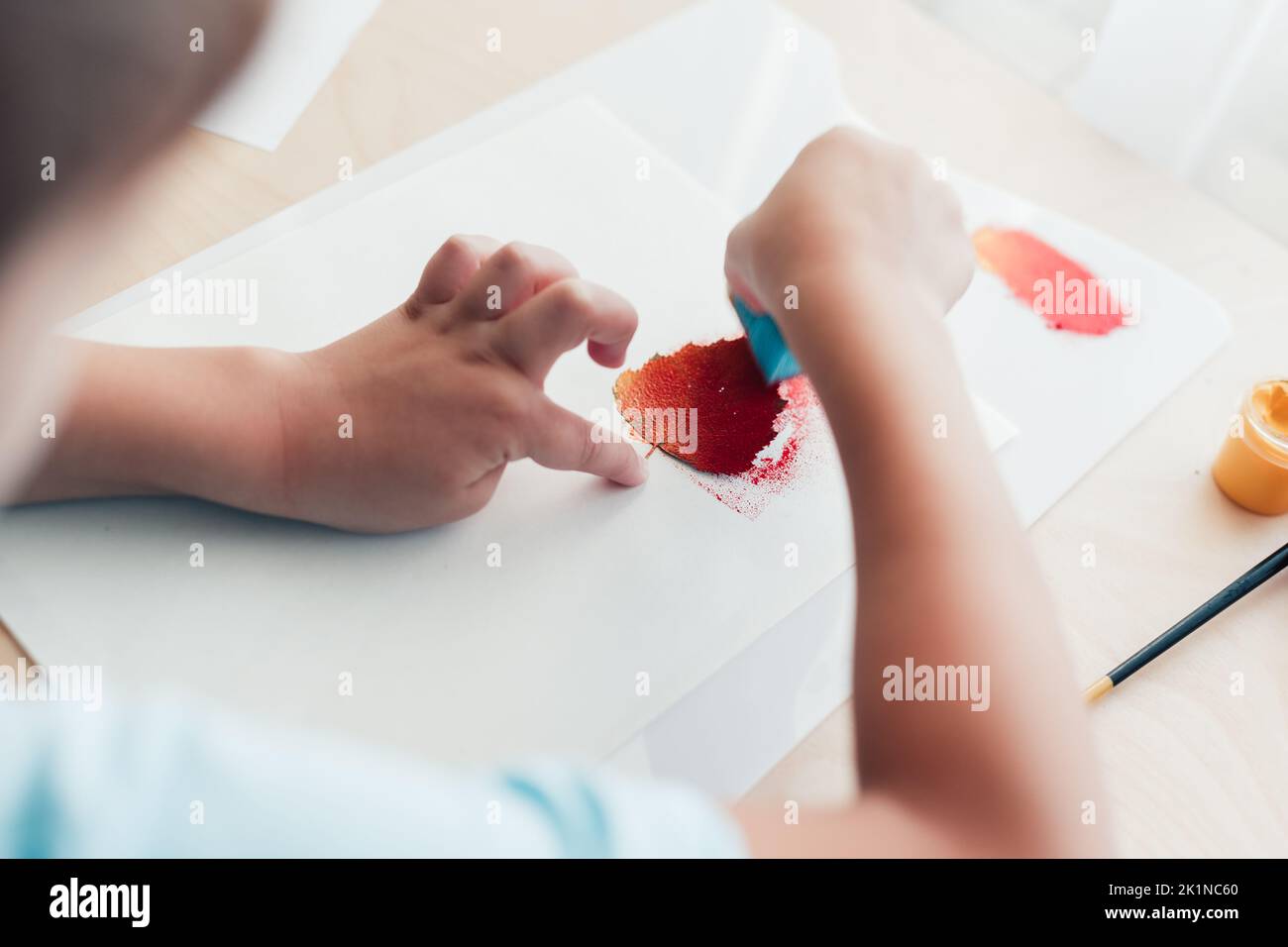 Cute child sitting at desk and making picture from colored birch leaves ...
