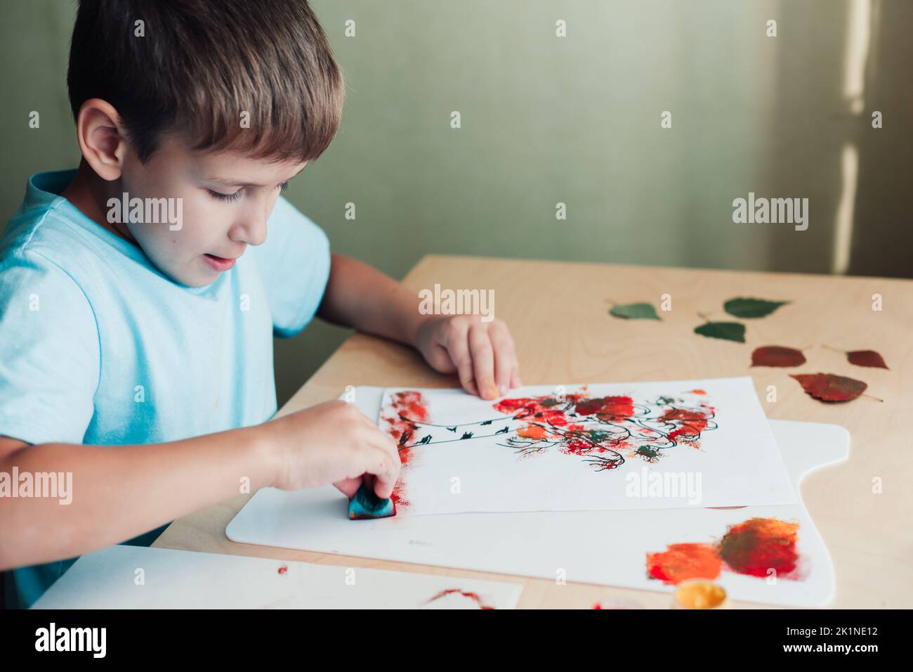 Cute child sitting at desk and making picture from colored dry birch ...