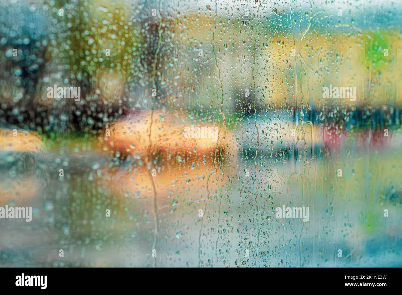 Blurred city view from window, rain drops, evening street traffic, car ...